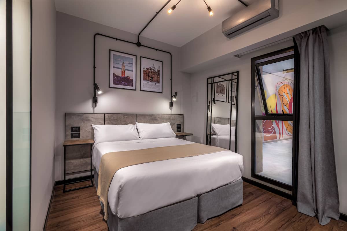 Quarto de hotel moderno com uma cama grande, mesas de cabeceira, janela com vista e obras de arte nas paredes.