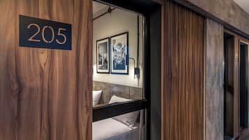 Quarto de hotel com parede de madeira, placa com o número '205', uma cama, um criado-mudo e duas molduras na parede.