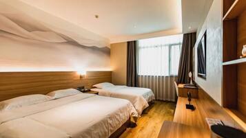 Quarto de hotel com duas camas, piso de madeira, escrivaninha e uma janela grande com cortinas.