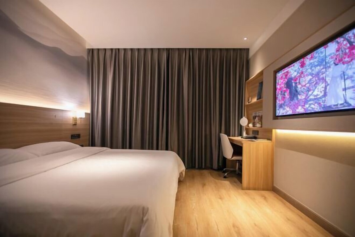 Quarto de hotel com uma cama, escrivaninha, cadeira, televisão e cortina.