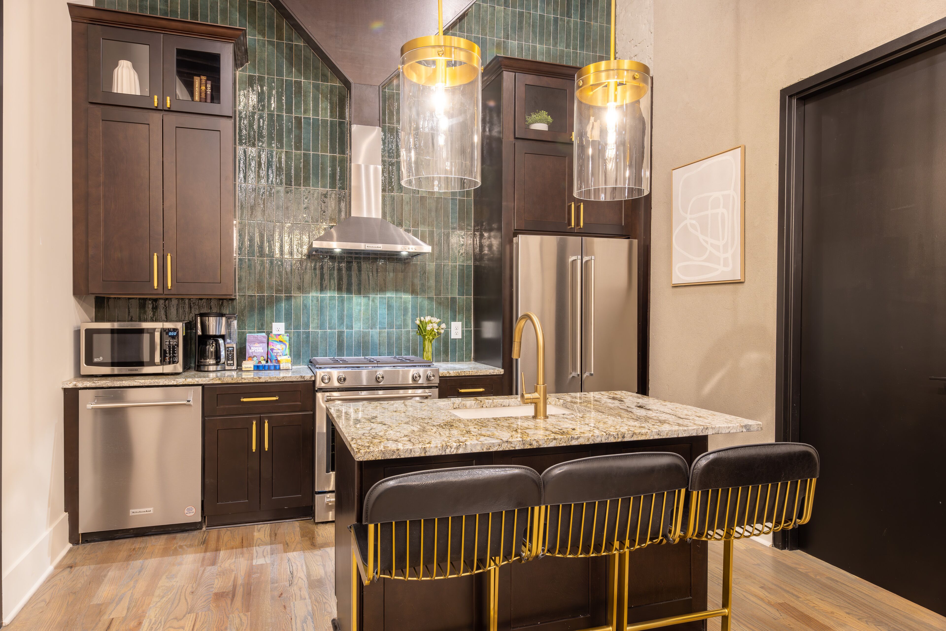 Cozinha moderna com armários escuros, eletrodomésticos de aço inoxidável, bancada de mármore e área de bar com banquetas.