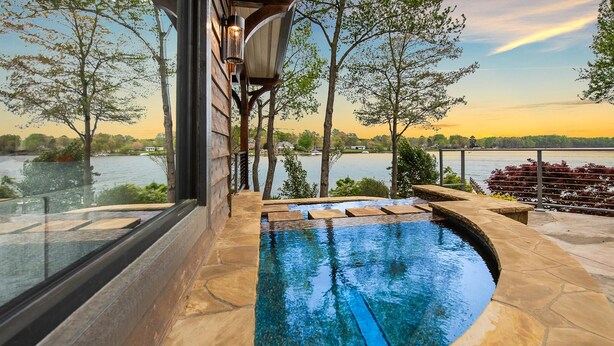 Piscina com ladrilhos de pedra e vista para um lago ao pôr do sol.