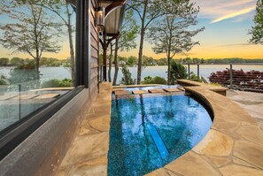 Piscina com ladrilhos de pedra e vista para um lago ao pôr do sol.