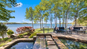 Uma área de piscina com vista para um lago, rodeada por árvores e assentos ao ar livre.