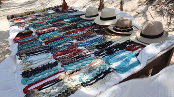 Diversos colares e chapéus coloridos expostos sobre uma mesa ao ar livre.