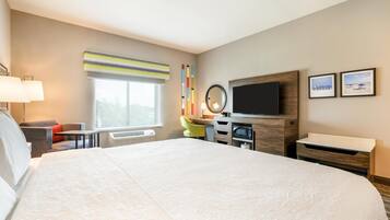 Quarto de hotel com uma cama grande, uma mesa com cadeira, televisão e janela com persianas.