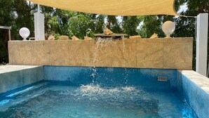 Piscina com cascata, rodeada por um muro de pedra e um toldo.