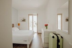 Quarto com cama, cômoda, espelho e mala.