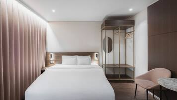 Quarto de hotel moderno com uma cama grande, área de estar com uma mesa, guarda-roupa e espelho.