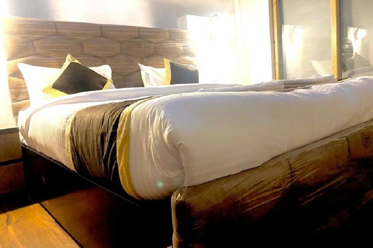 Cama com cabeceira de madeira, roupa de cama branca e várias almofadas.