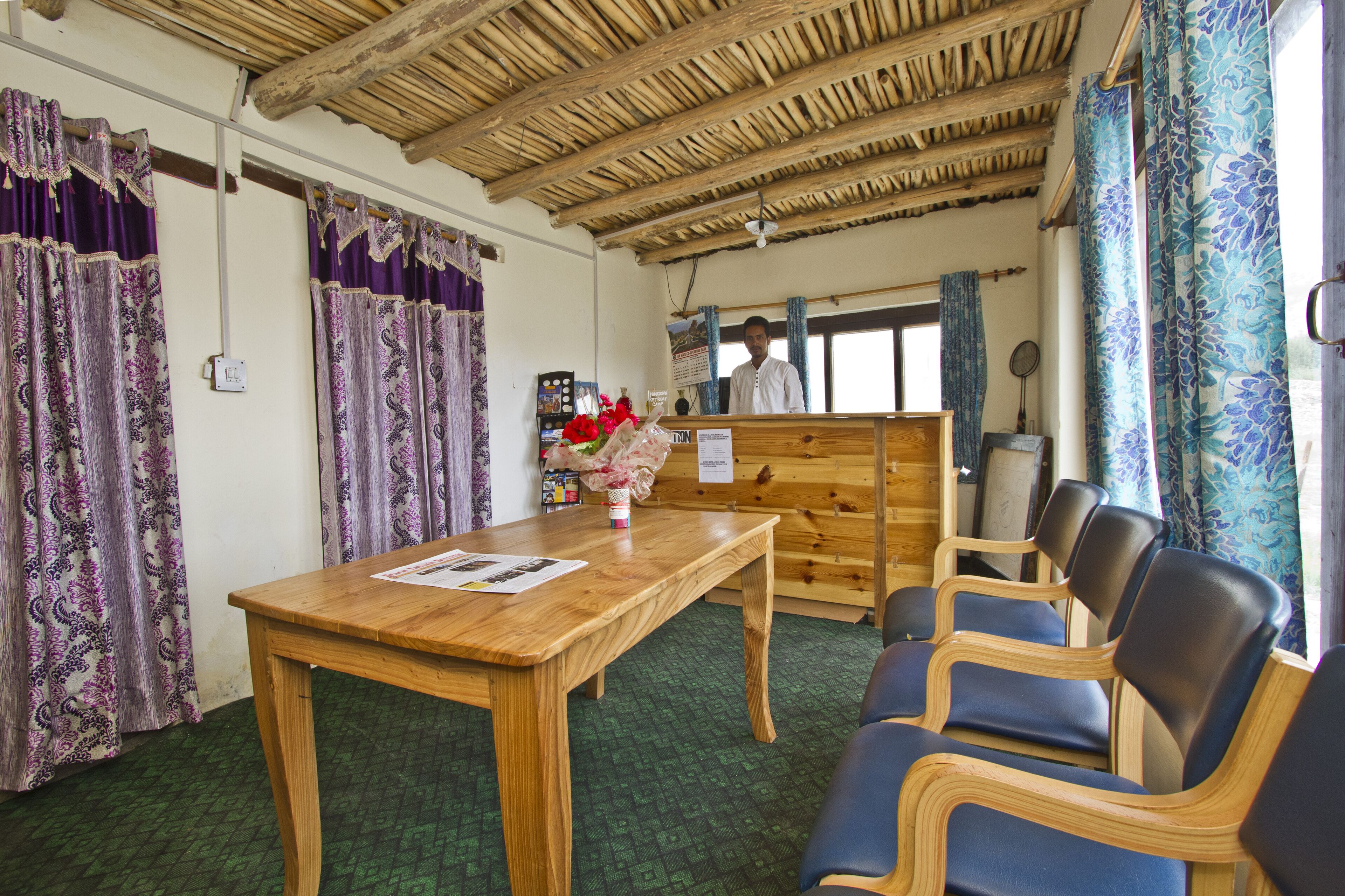 Uma mesa de madeira com cadeiras, um mural de avisos e uma janela com cortinas.