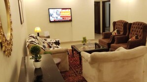Uma sala de estar com sofá, poltronas, mesa de centro, televisão e uma pequena planta.