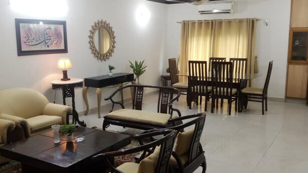 Uma sala de estar com sofá, mesa de centro, mesa de jantar com cadeiras, abajur e espelho fixado na parede.