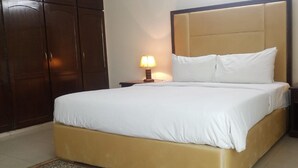 Quarto de hotel com uma cama grande, duas mesas de cabeceira com luminárias, um guarda-roupa e um tapete.