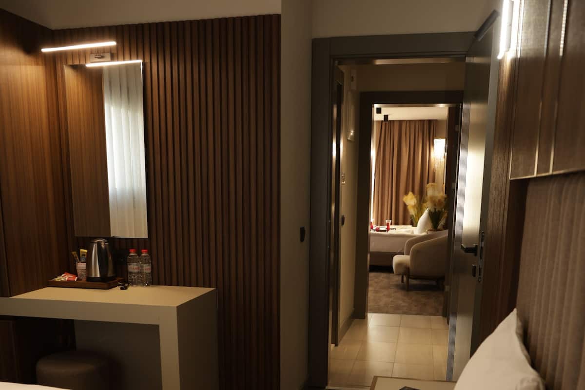 Quarto de hotel com uma cama, uma escrivaninha com luminária, uma cadeira e vista para uma sala de estar.