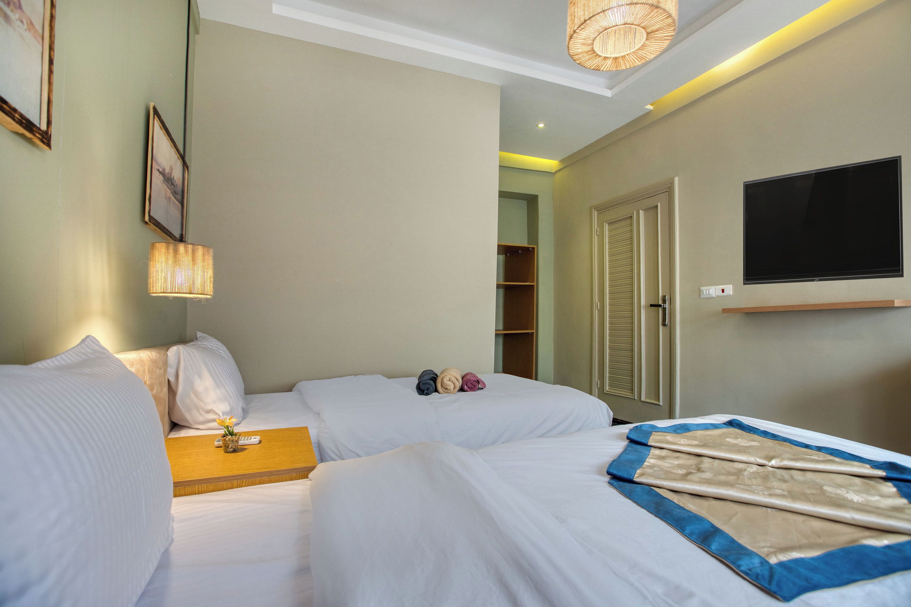 Quarto de hotel com duas camas, uma televisão, uma mesa de cabeceira e um guarda-roupa.