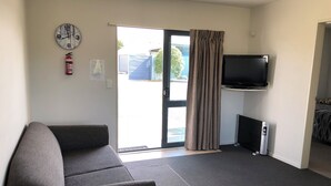 Uma sala de estar com sofá cinza, televisão de tela plana na parede e porta de vidro deslizante que dá para uma área externa.