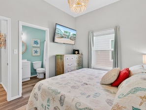 Quarto com cama, cômoda, televisão na parede e janela com cortinas.