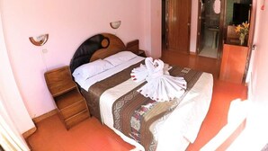 Quarto com cama, mesa de cabeceira de madeira, luminária na parede, área de chuveiro e porta de madeira.