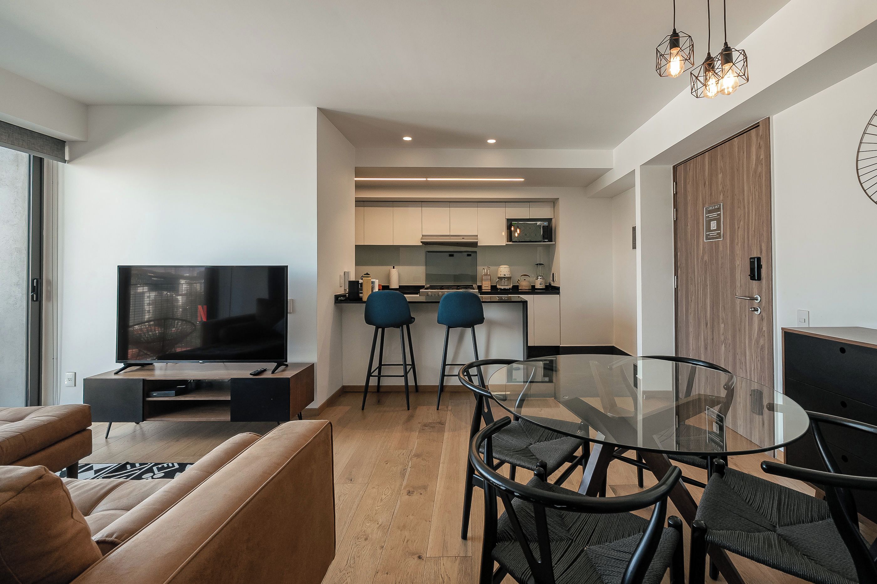 Uma sala de estar moderna com televisão de tela plana, uma mesa de jantar de vidro e um sofá.