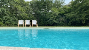 Piscina com três espreguiçadeiras brancas.