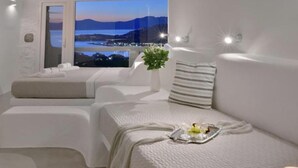 Um spa moderno com uma cama, uma cadeira de massagem e vista para a paisagem costeira.