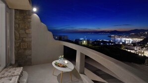 Varanda com mesa e cadeiras, com vista para um horizonte costeiro noturno.