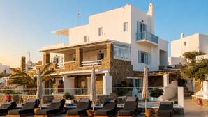 Um hotel moderno com piscina, cadeiras de lounge e um céu azul límpido.