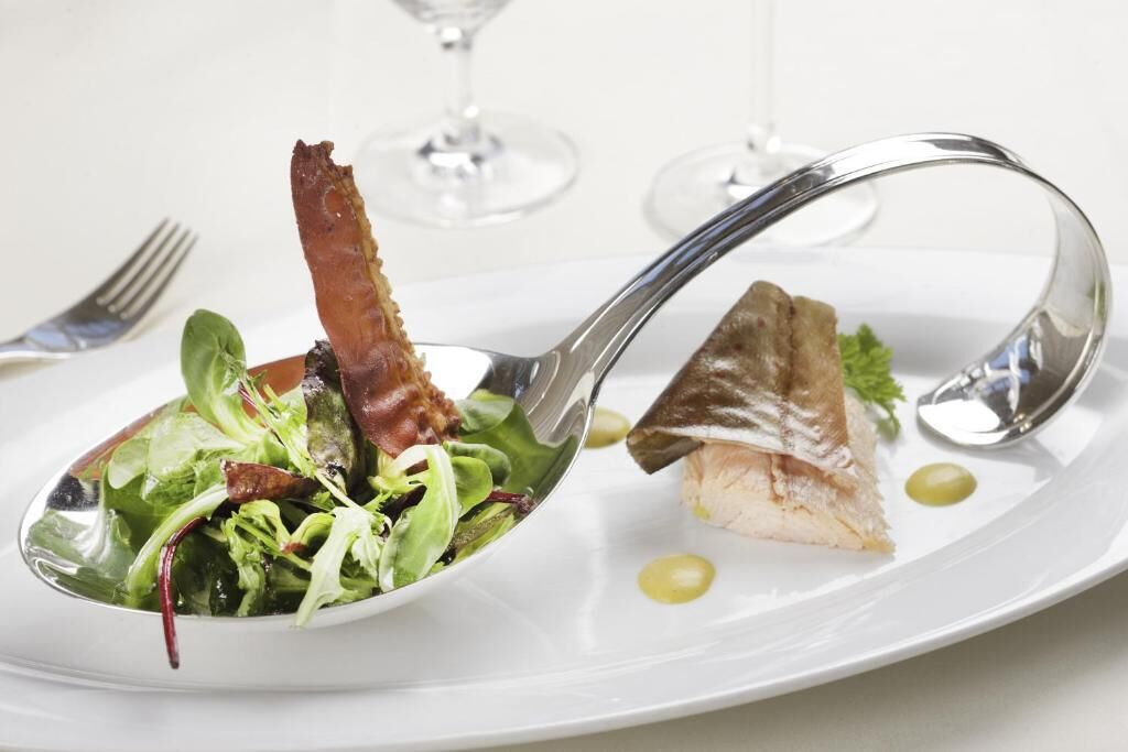 Um prato branco com salada, um pedaço de peixe e um garfo.