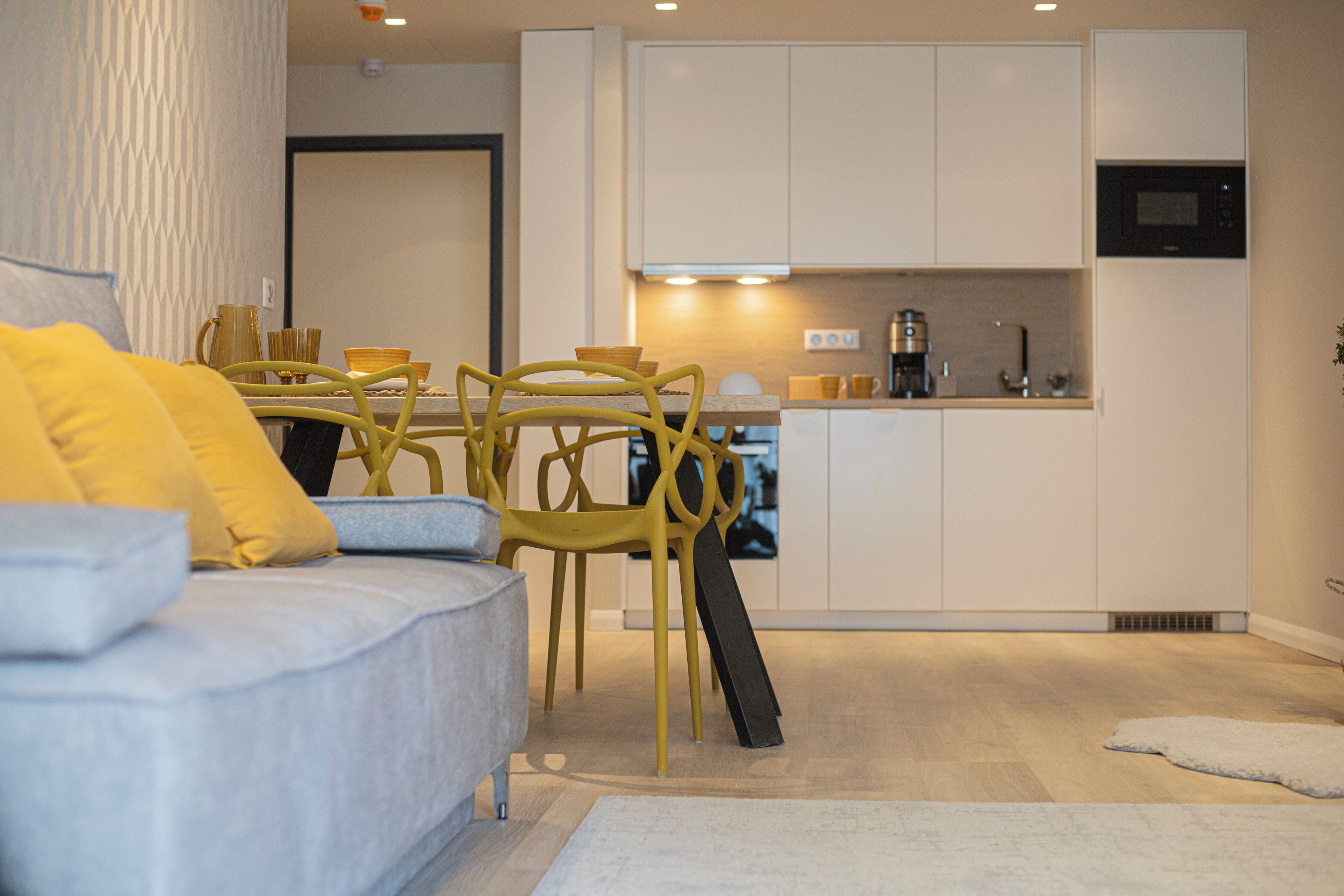 Uma sala de estar moderna com um sofá, cadeiras amarelas e uma área de jantar com mesa e cadeiras.