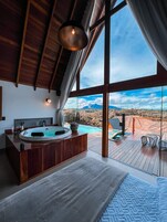 Uma casa de banho moderna com toucador de madeira, uma banheira grande e vista para uma paisagem montanhosa através de amplas janelas.
