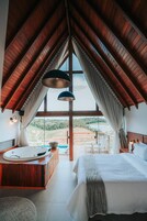 Quarto com uma grande janela, teto de madeira e cama com colcha branca.