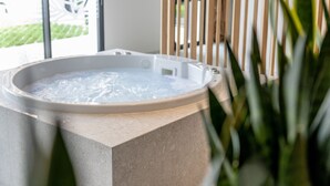 Uma banheira de hidromassagem com vista para um jardim e um edifício ao fundo.