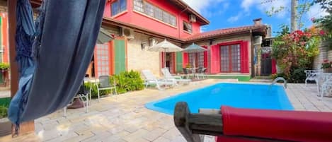 Área da piscina com uma cadeira vermelha, uma rede e uma piscina.