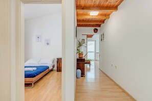 Um corredor estreito com piso de madeira, uma cama com roupa de cama azul e uma mesa com uma planta.
