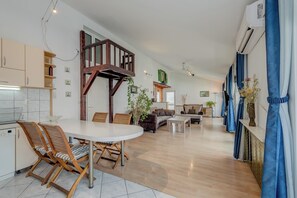 Cozinha moderna com armários brancos, mesa de jantar com cadeiras, escada e sala de estar com sofás e mesa de centro.