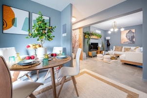 Uma sala de estar moderna com área de jantar, apresentando uma mesa redonda, cadeiras brancas e um vaso com planta.