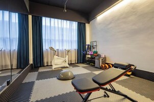 Quarto com cadeira de massagem, bicicleta ergométrica e um pequeno espaço para exercícios.