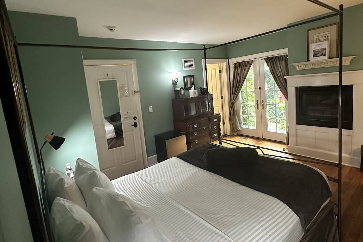 Um quarto com uma cama, penteadeira, espelho, televisão e uma janela com cortinas.