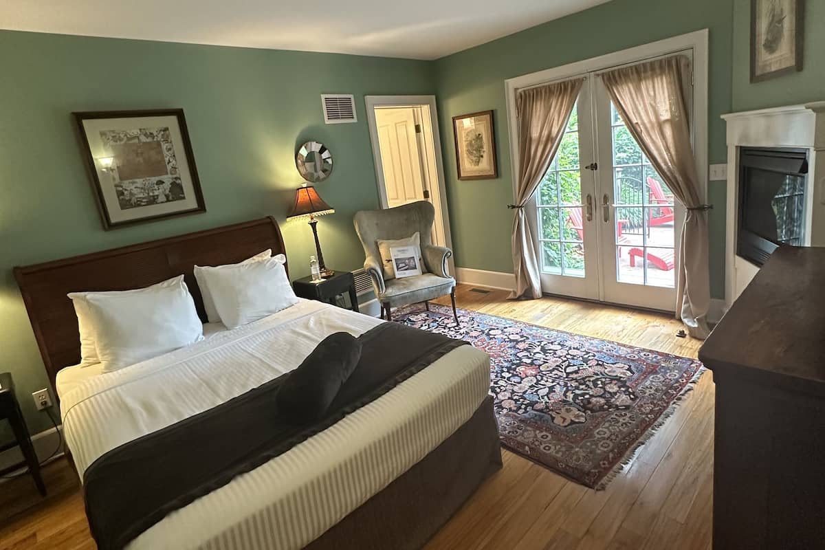 Quarto com cama grande, cadeira, lareira e vista para o exterior.