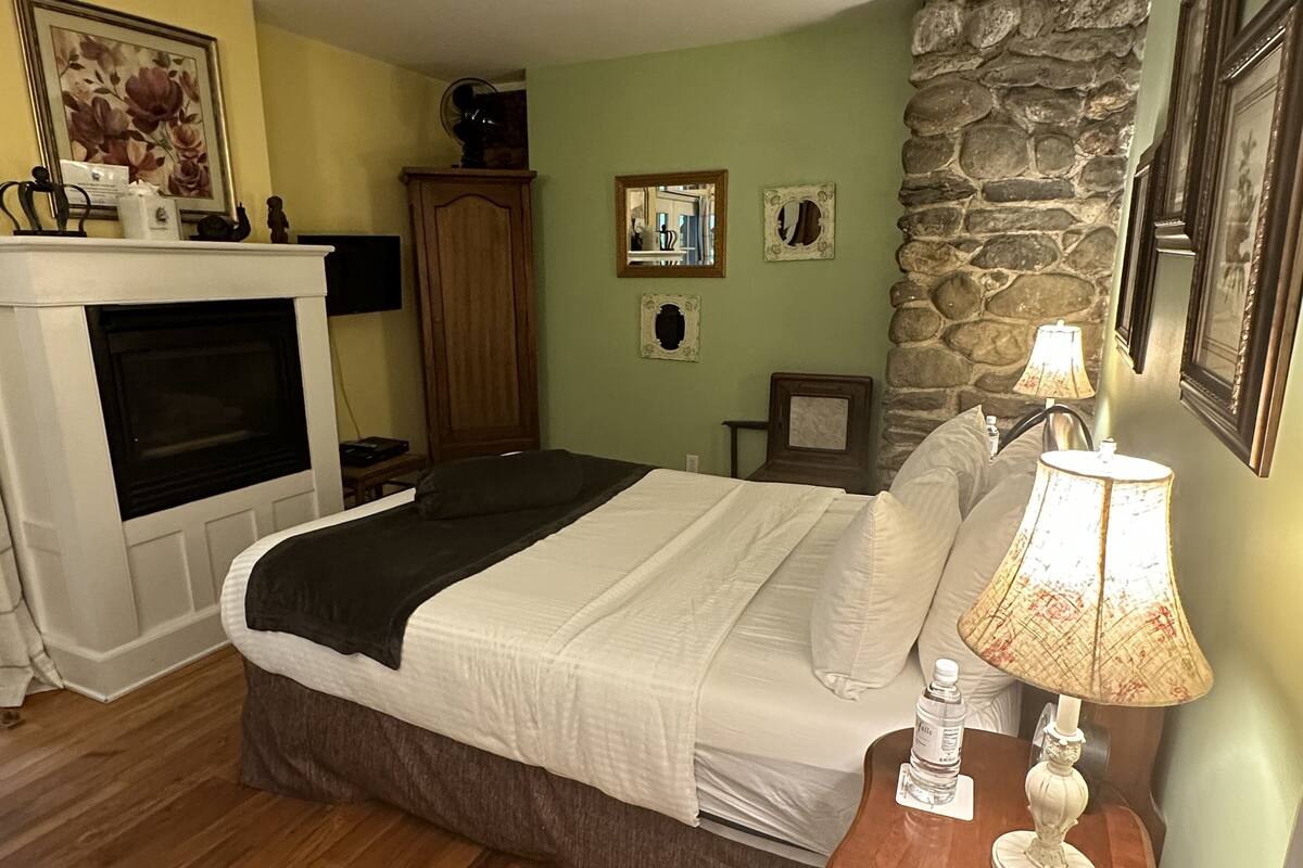 Quarto com uma cama, mesa de cabeceira com luminária, lareira e parede de pedra.