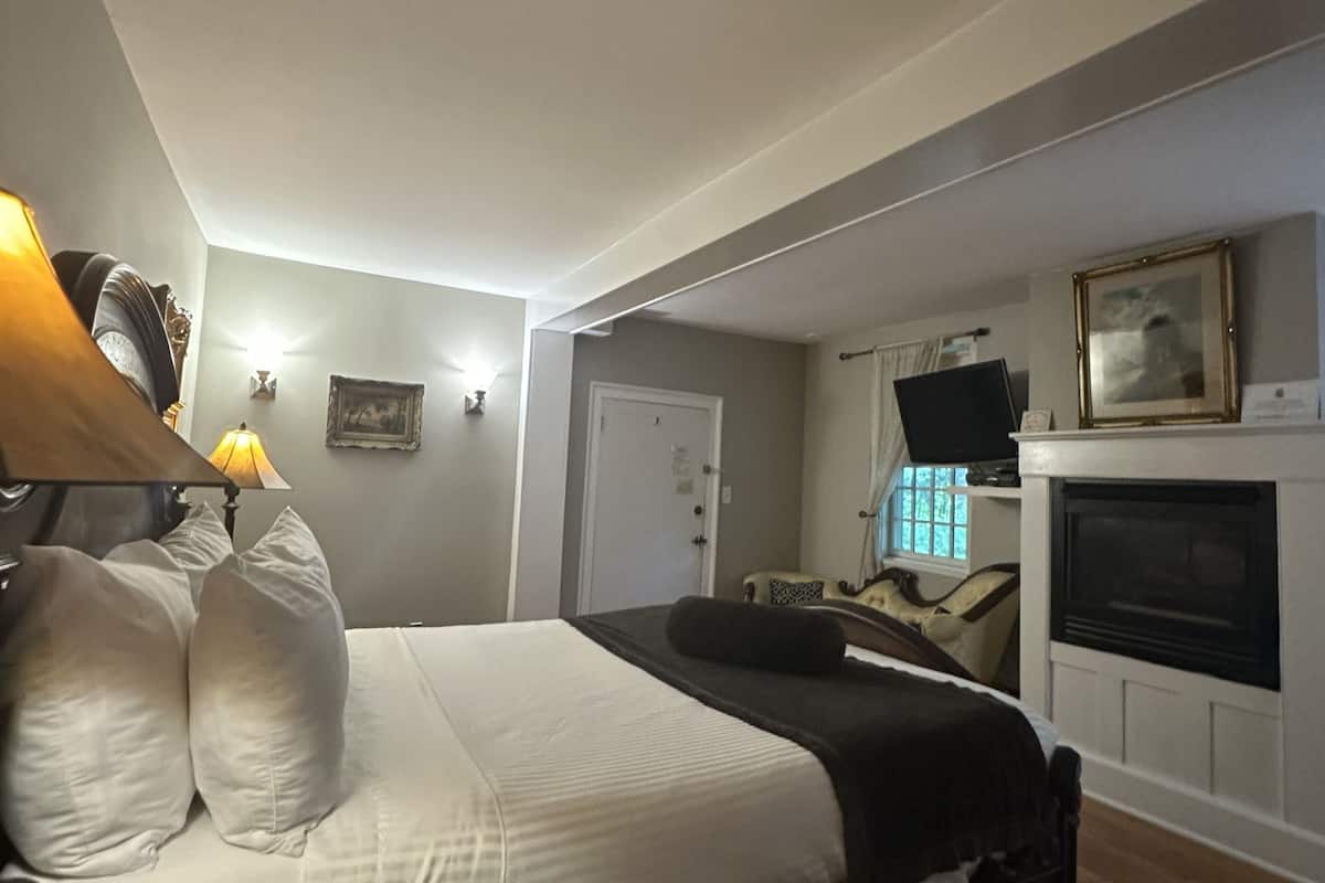 Quarto com cama, mesa de cabeceira, luminária, lareira e porta.