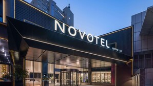 Entrada de um hotel com uma placa grande da NOVOTEL, portas de vidro e um design arquitetônico moderno.