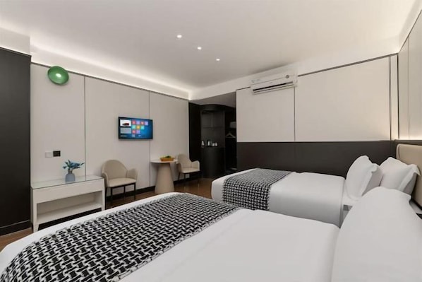 Quarto de hotel moderno com duas camas, televisão, escrivaninha e uma cadeira.