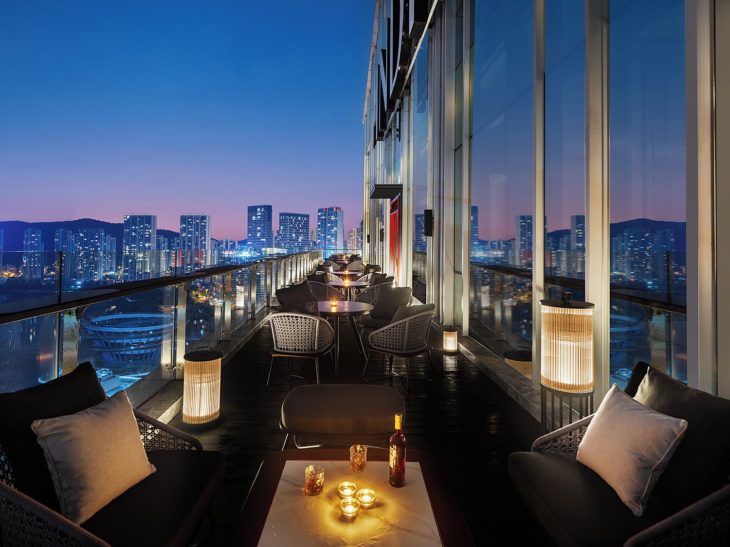 Um bar no terraço com vista para a cidade, equipado com cadeiras e mesas, e uma garrafa de vinho sobre uma mesa.