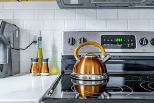 Cozinha com fogão de aço inoxidável, duas garrafas de tempero e uma chaleira.