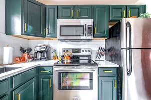 Cozinha com armários verdes, geladeira de aço inoxidável, micro-ondas, fogão e forno embutido.