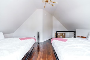 Quarto com duas camas, piso de madeira, ventilador de teto e uma mesinha de cabeceira.