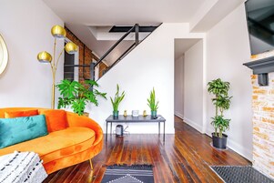 Uma sala de estar moderna com um sofá laranja curvo, um tapete preto e branco e uma escada com corrimão preto.