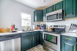 Cozinha moderna com armários verde-escuros, eletrodomésticos de aço inoxidável e painel de azulejos brancos.